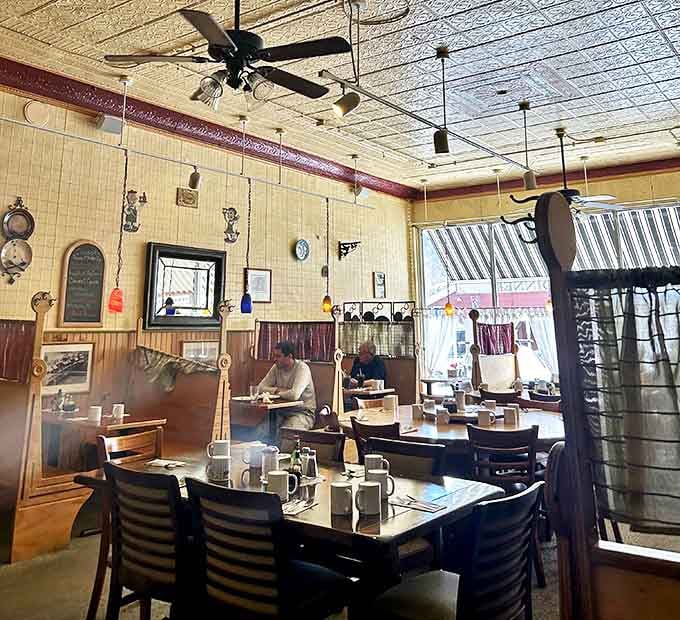 Morning light streams through windows, illuminating cozy wooden booths where locals linger over coffee. The ornate ceiling adds unexpected character to this hometown haven.