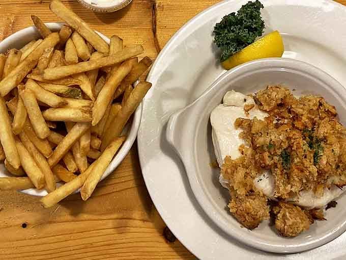 Behold the star attraction: baked haddock with its golden Ritz cracker crown, sitting regally beside hand-cut fries like seafood royalty.