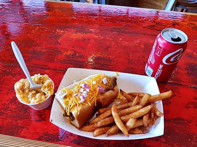 Hot dog perfection doesn't need fancy trappings&mdash;just cheese, onions, crispy fries, and a cold drink on a weathered red table.