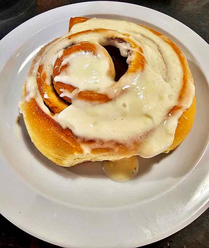 The legendary cinnamon roll that's caused more double-takes than a celebrity sighting. This spiral of sweet perfection is practically swimming in glorious icing.
