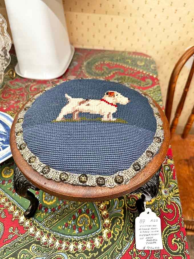 A needlepoint terrier sits regally on its throne, silently judging your decorating choices while waiting for the perfect home.