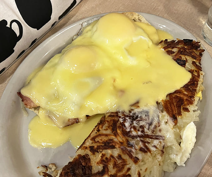 Eggs Benedict that defies gravity &ndash; hollandaise sauce cascading like a yellow waterfall over perfectly poached eggs and crispy hashbrowns. Breakfast architecture at its finest.