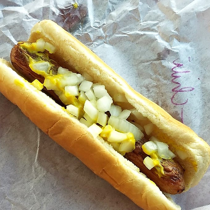 Hot dog perfection: crisp-skinned, nestled in a soft bun, topped with diced onions and mustard. Simple pleasures are often the best.