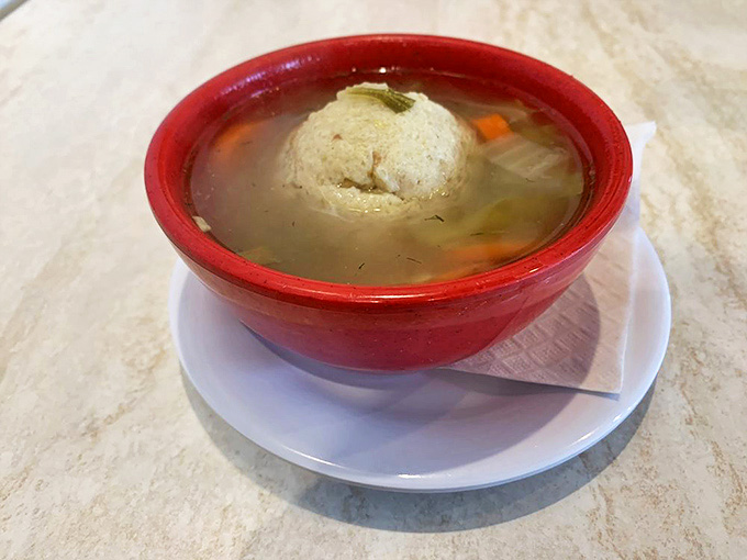 The matzo ball floats like a planet in a galaxy of golden broth &ndash; not too dense, not too light, achieving that perfect grandmotherly balance.