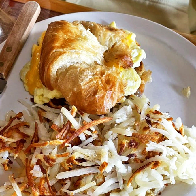 Breakfast engineering at its finest: a golden croissant cradling eggs and cheese, with hash browns so crispy they deserve their own fan club.