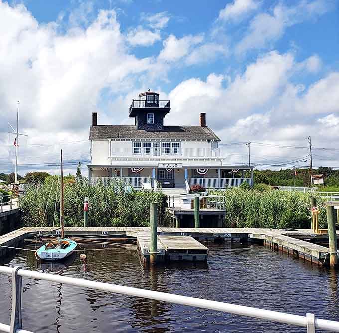 The Tucker's Island Lighthouse stands sentinel over the harbor, its white facade and dark lantern room a beacon of maritime history against the cloud-dotted sky.