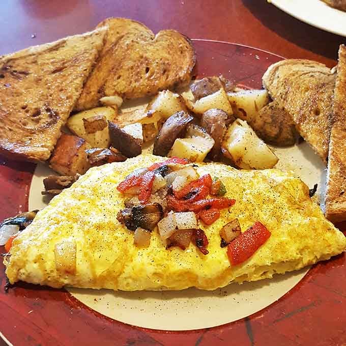 A perfectly executed omelet bursting with fresh vegetables and melted cheese, flanked by crispy home fries and toast &ndash; breakfast architecture at its finest.