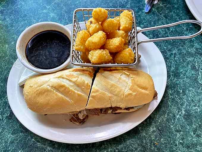 A French dip sandwich that means business, paired with golden tater tots that crunch like autumn leaves—comfort food poetry on a plate.