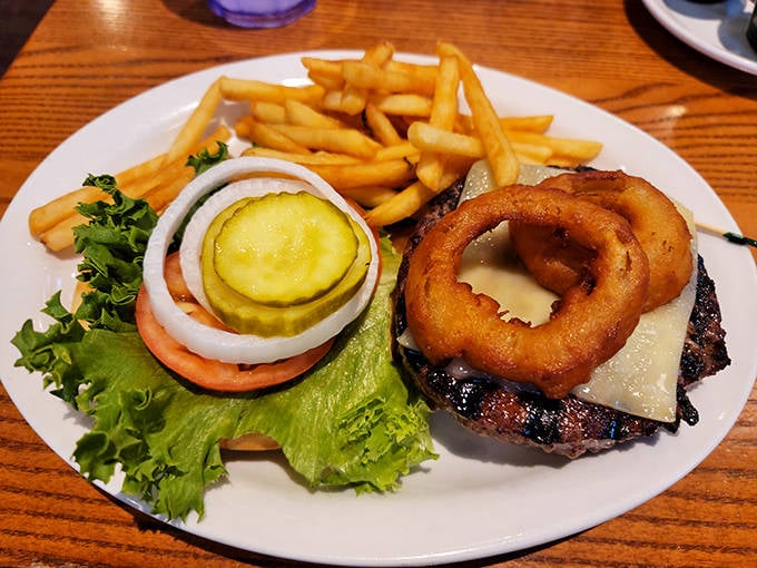 The burger arrives wearing its onion ring crown proudly, a monarch of lunch options that demands both hands and napkins.
