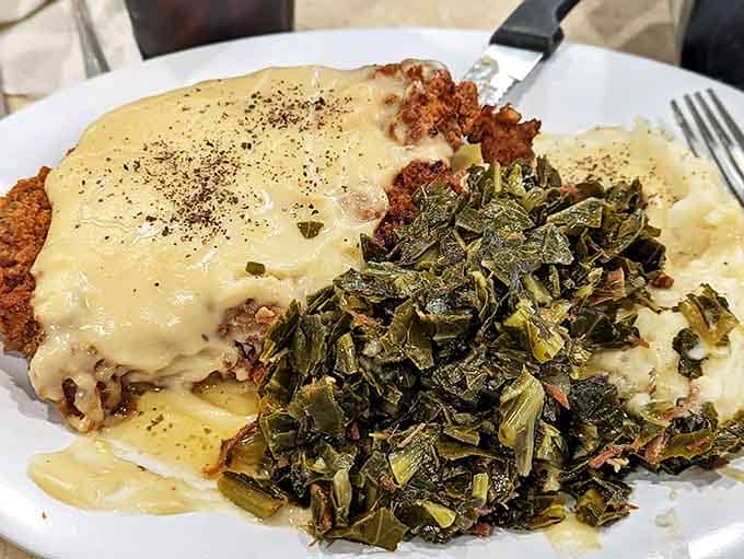 Country fried steak swimming in gravy with collard greens standing by. This plate has more Southern charm than a Tennessee Williams play.