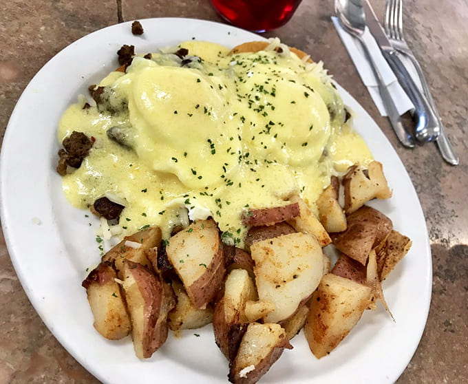 Eggs Benedict reimagined &ndash; golden hollandaise cascading over perfectly poached eggs atop what appears to be their famous hash, with home fries standing guard.