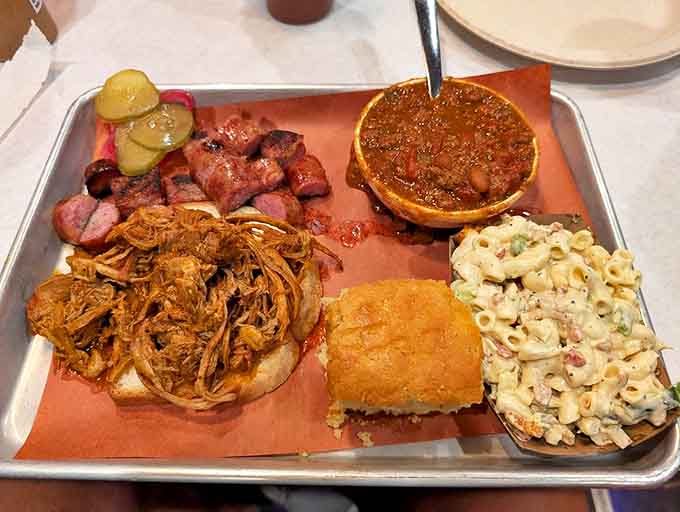 BBQ sampler heaven—pulled pork, sausage, beans, and mac and cheese on one tray. The metal serving plate says "we mean business."
