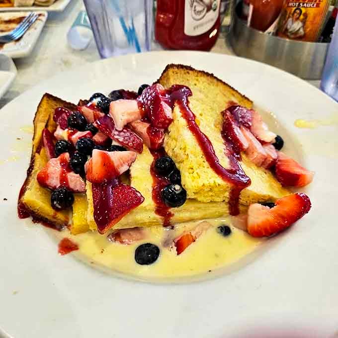 French toast that's having an identity crisis as dessert, crowned with berries that pop with such freshness they might have been picked minutes ago.