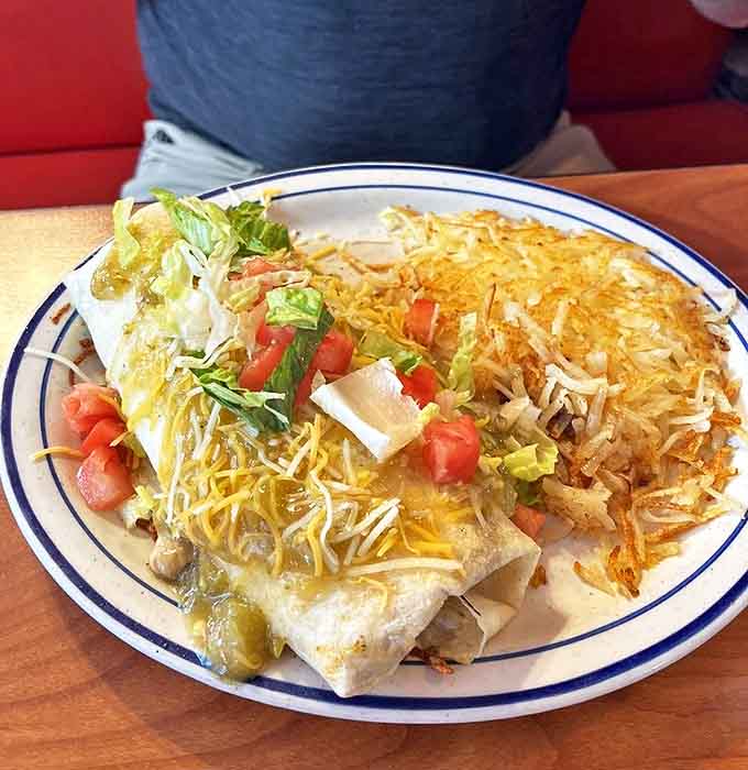 Breakfast burrito architecture that defies gravity and common sense. Cheese, lettuce, and green chili creating a masterpiece that requires both hands and napkins.