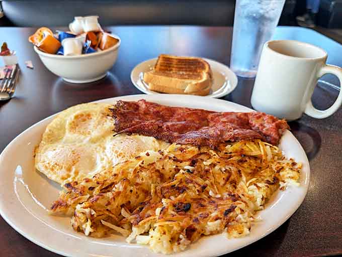 The breakfast trinity: perfectly cooked eggs, crispy hash browns, and bacon that would make even vegetarians reconsider their life choices.