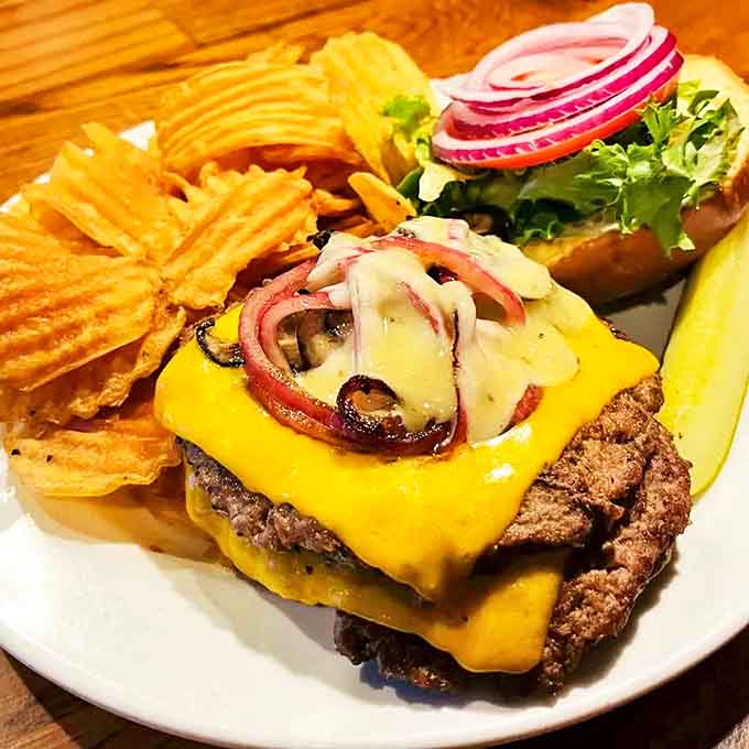 A burger that requires both hands, a stack of napkins, and absolutely no first-date jitters. That melted cheese cascade is what dreams are made of.