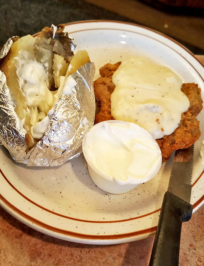Chicken fried steak smothered in country gravy alongside a loaded baked potato. A plate that answers the eternal question: "What does Kansas taste like?"