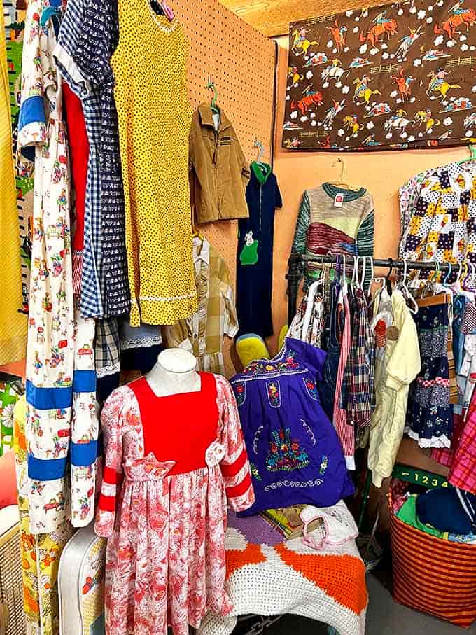 A kaleidoscope of vintage children's clothing awaits new little shoulders. That embroidered Mexican dress probably has more stories than the books nearby.
