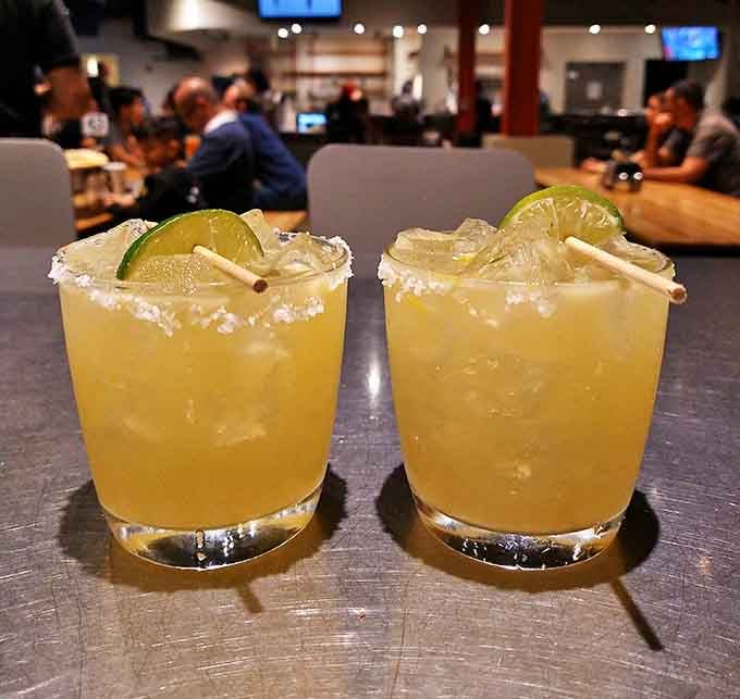 Two margaritas with salt-rimmed glasses stand ready for duty &ndash; the perfect liquid sidekicks to tame the mighty pizza slices.