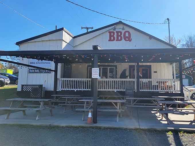 The unassuming white clapboard exterior of Barbeque Exchange, where picnic tables await hungry patrons seeking smoky perfection.