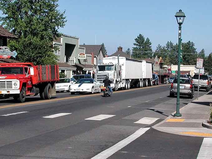 Mountain scenery surrounds you as vintage cars, motorcycles, and heavy trucks roll through this charming, sun-drenched small town street.