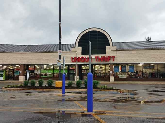 The iconic arched entrance of Unique Thrift beckons like a retail rainbow after rain, promising treasures beyond those bright blue bollards and bold red letters.