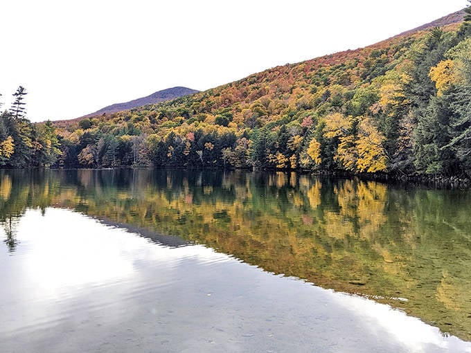 Fall foliage creates a perfect mirror image on Emerald Lake's still waters, showcasing Vermont's autumn splendor in vibrant, reflected glory.