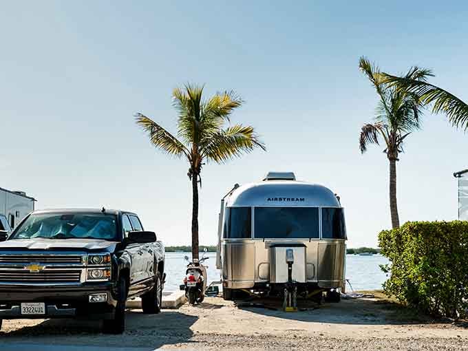 That gleaming Airstream knows it's living its best life, parked where the water meets endless blue skies.