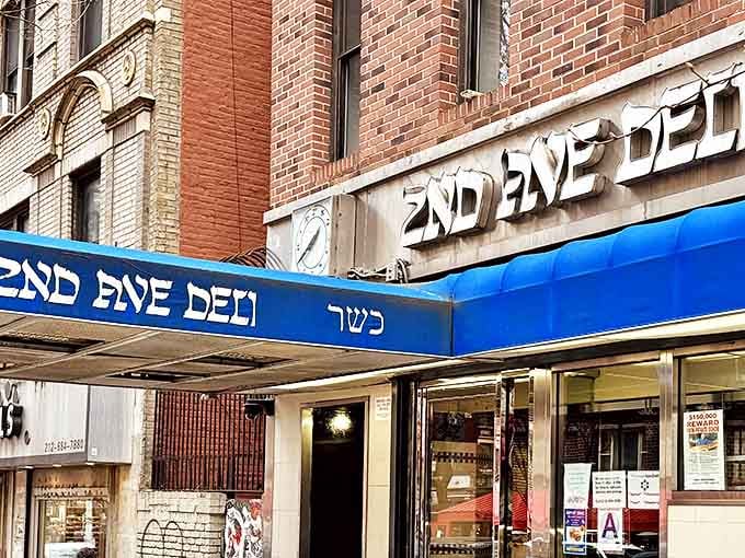 The iconic blue awning of 2nd Ave Deli stands as a beacon of hope for pastrami pilgrims, promising sandwich salvation in a city of endless food options.