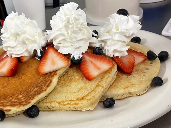 Fluffy pancakes lined up like edible soldiers, crowned with strawberries and whipped cream rosettes that belong in a museum.