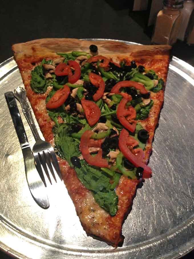 Fresh veggies crown this towering slice like a garden decided to vacation on perfectly baked dough.