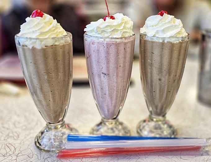 Three milkshakes standing tall with whipped cream and cherries, ready for their close-up and your spoon.