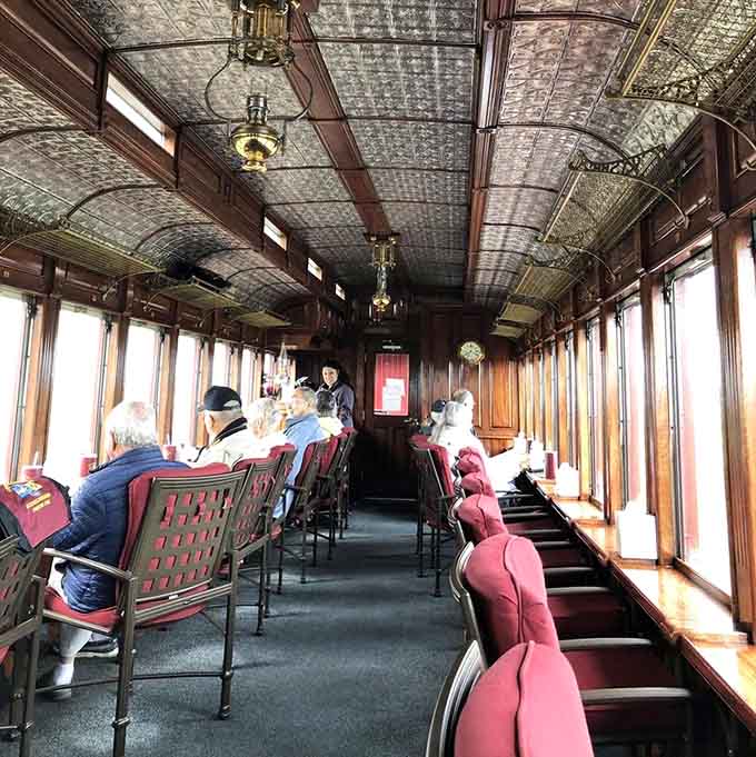 The elegant parlor car interior features ornate pressed-tin ceilings and polished wood that would make any luxury train jealous.