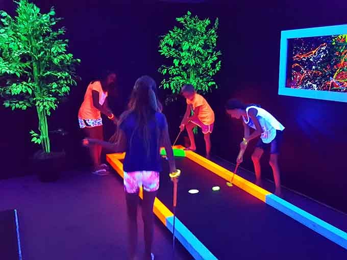 Young players navigate the glowing fairways with concentration, their white shirts transforming into beacons of fluorescent light.