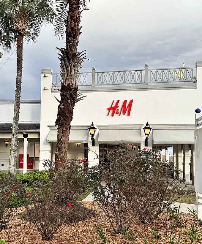 H&M's bright red signage pops against the white building, with palm trees standing guard. Nature and fashion coexist peacefully in this retail ecosystem.