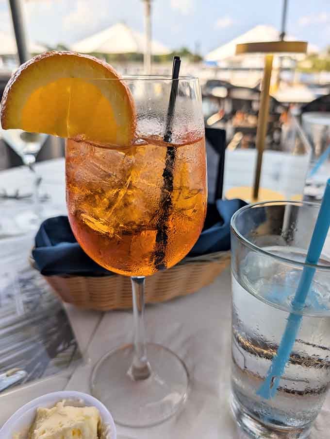 An Aperol spritz catching the golden hour light while boats drift by in the background serenely.