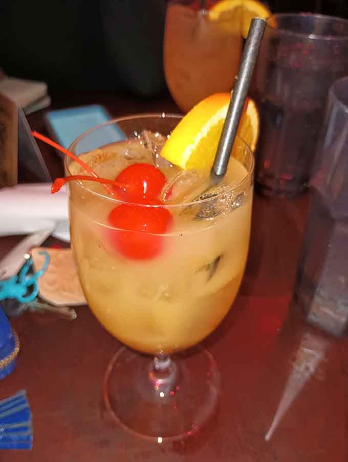 A tropical cocktail garnished with fruit and a cherry brings vacation vibes to your literary-themed lunch experience.