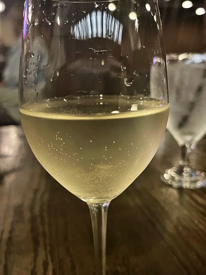 A glass of chilled white wine catching the light just so. Like liquid sunshine waiting to complement whatever delicious choice you've made.