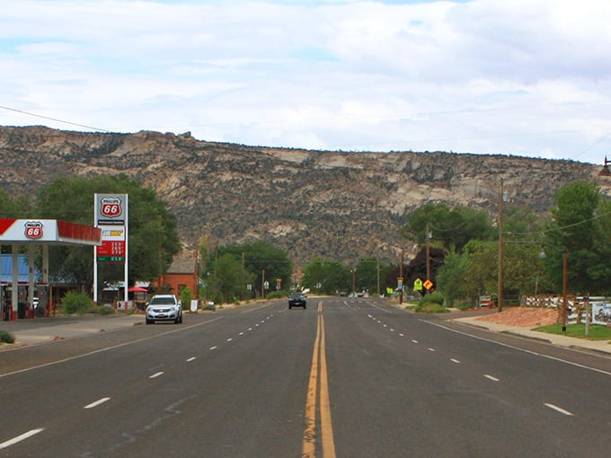 The road stretches toward geological wonders, with Utah's signature layered cliffs standing guard. Adventure lies just beyond that next bend.