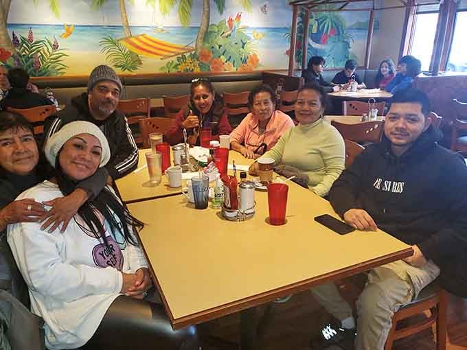Happy diners gathered around tables with tropical murals behind them capture the welcoming community atmosphere that keeps people returning.