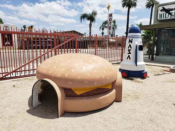 A giant cheeseburger playhouse sits next to a NASA rocket, because childhood dreams know no logical boundaries here.