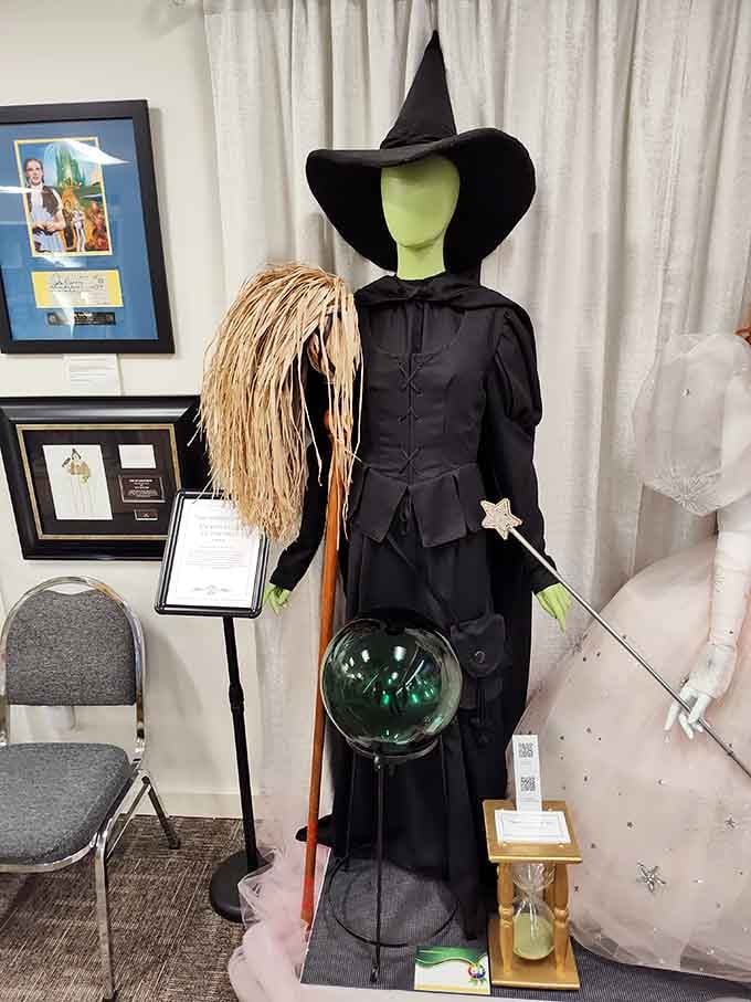The Wicked Witch stands ready with broom and crystal ball, looking surprisingly fabulous in basic black.