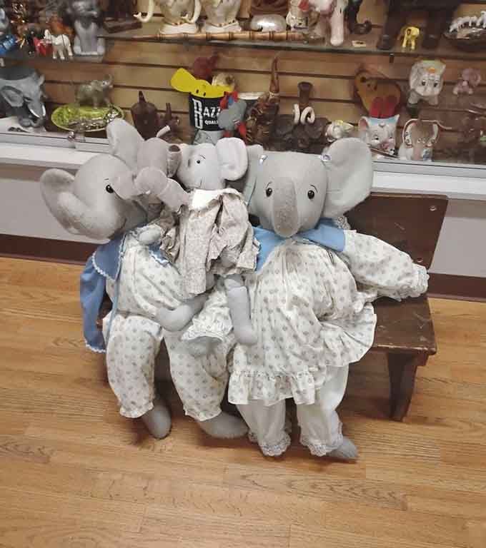 Vintage stuffed elephants in Victorian dress sit primly on a bench, adding a touch of genteel charm to the collection.