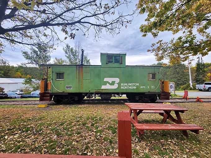 A Burlington Northern caboose rests among fall leaves, the kind of railroad relic that makes grown men suddenly interested in model trains again.