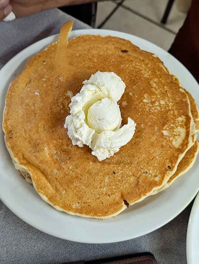 A pancake so perfectly golden it belongs in Fort Knox, crowned with a melting pat of butter that creates its own delicious currency.