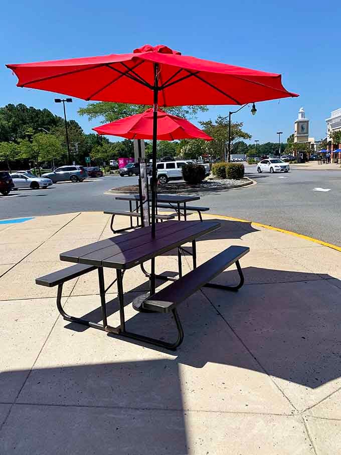 Al fresco dining area where shopping warriors rest their weary credit cards under cheerful red umbrellas before returning to retail battle.