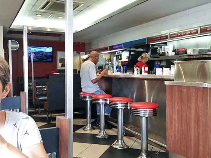 Classic diner counter seating where solo diners become regulars and strangers become friends over endless coffee.