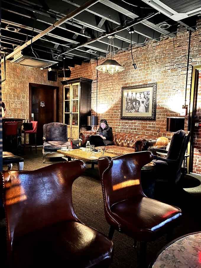 The lounge area with leather chairs and exposed brick offers a sophisticated spot to wait or just enjoy drinks.