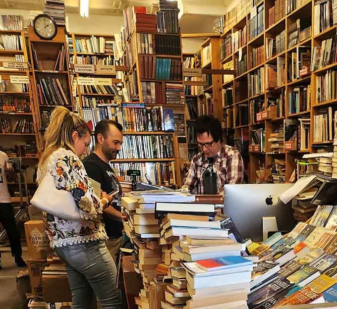 The checkout counter surrounded by towering book stacks, where your haul costs less than lunch out.