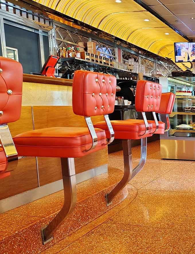 Retro counter seating with tufted orange vinyl lets solo diners watch the kitchen magic happen up close.